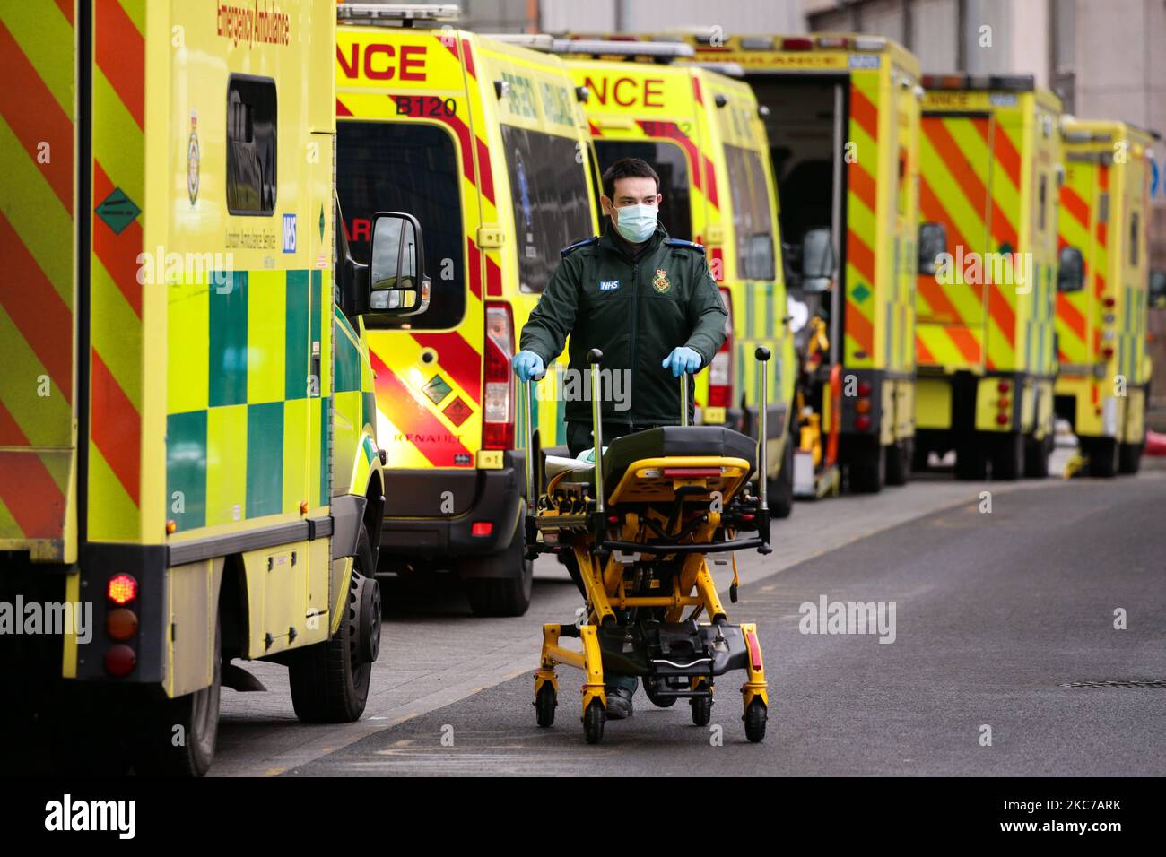 A paramedic wearing a face mask pushes a stretcher past ambulances ...