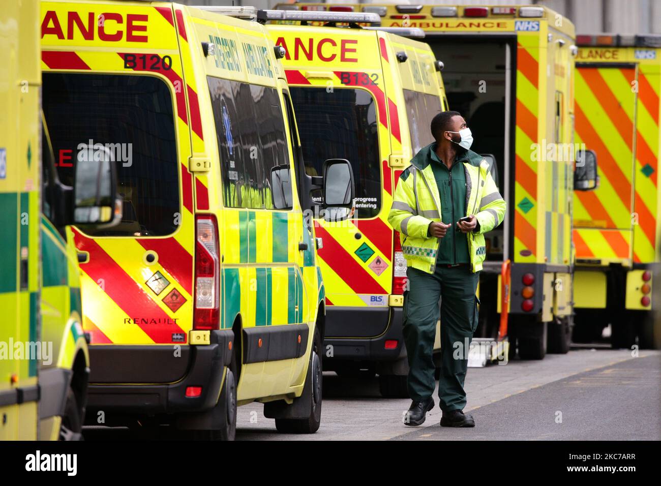 A paramedic wearing a face mask walks past ambulances parked outside ...