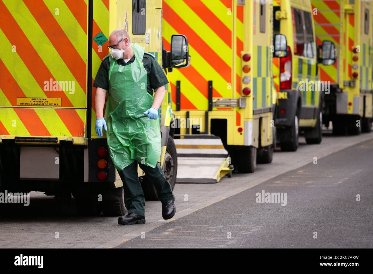 A paramedic wearing PPE walks beside ambulances parked outside the ...