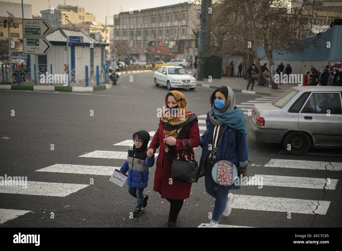 An Iranian family wearing protective face masks cross an avenue in ...