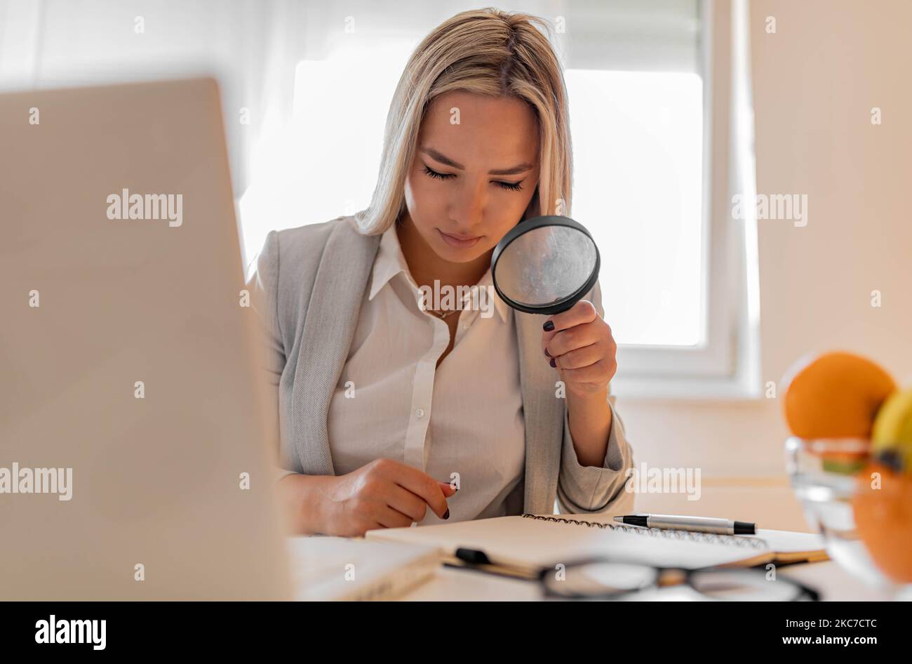 Curious young business woman looking through a magnifying glass in her ...