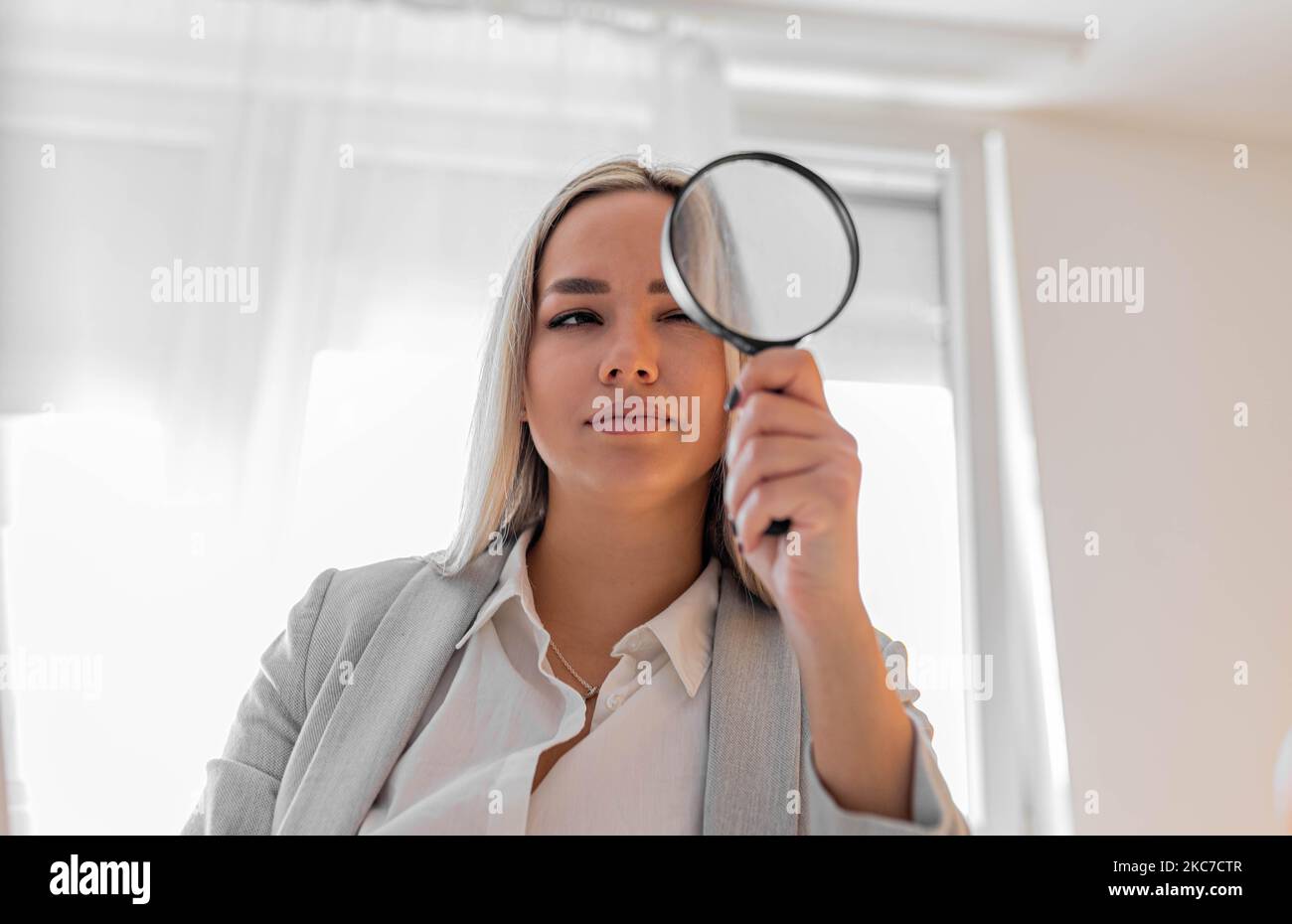 Curious young business woman looking through a magnifying glass in her ...