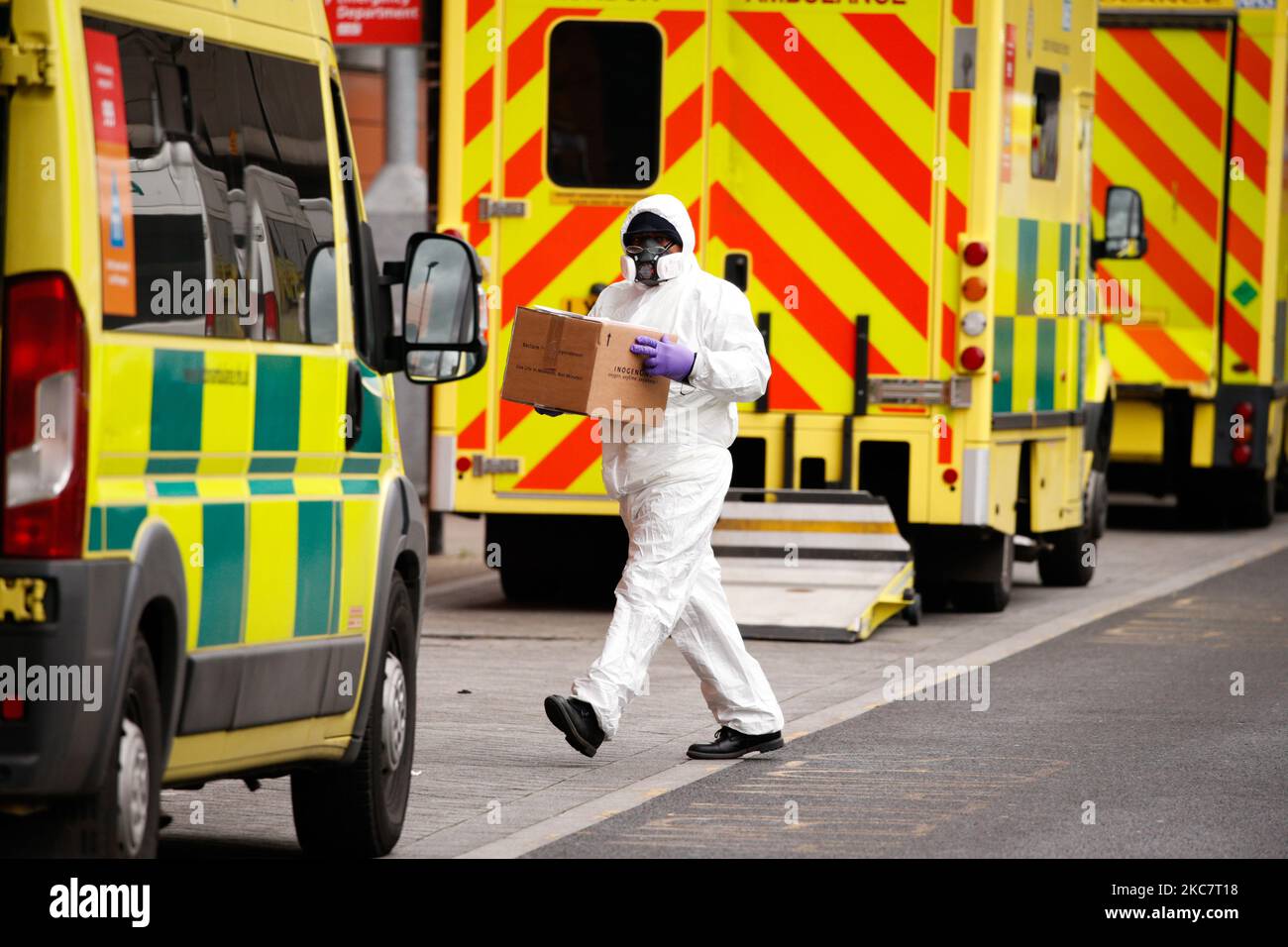 A delivery man wearing a PPE suit and respirator mask carries a package ...
