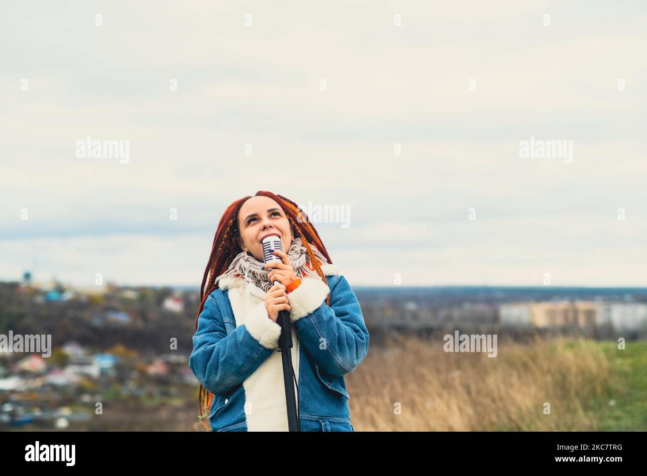 Young woman with dreadlocks singing into microphone in countryside ...