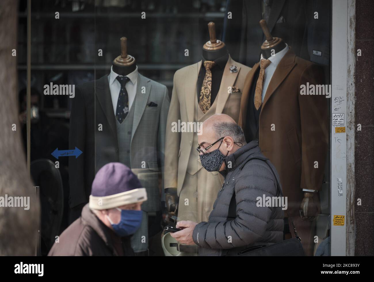 Two Iranian men wearing protective face masks walk past a dress shop ...