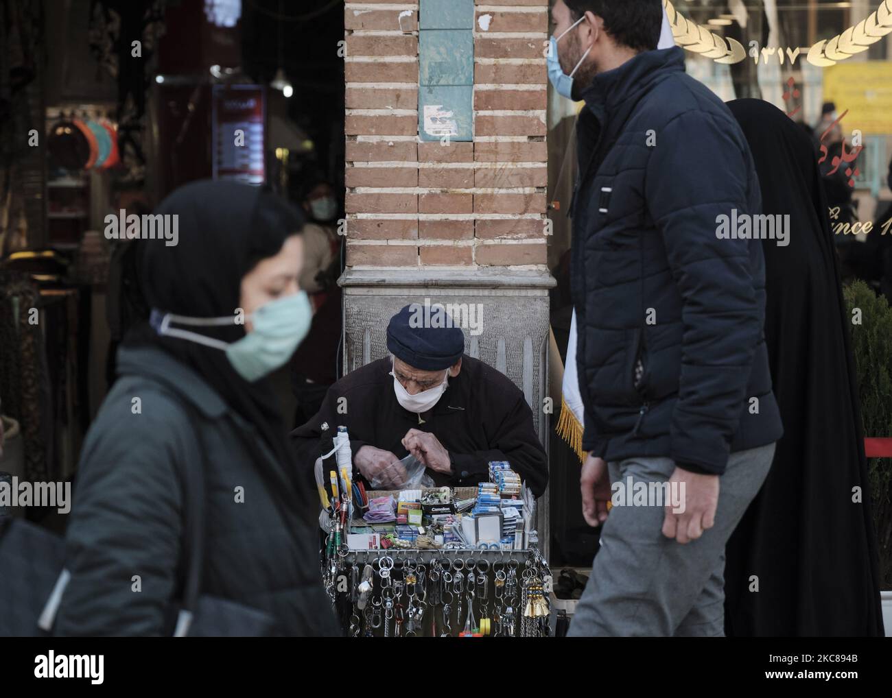 Iranian people wearing protective face masks walk past a vendor out of ...