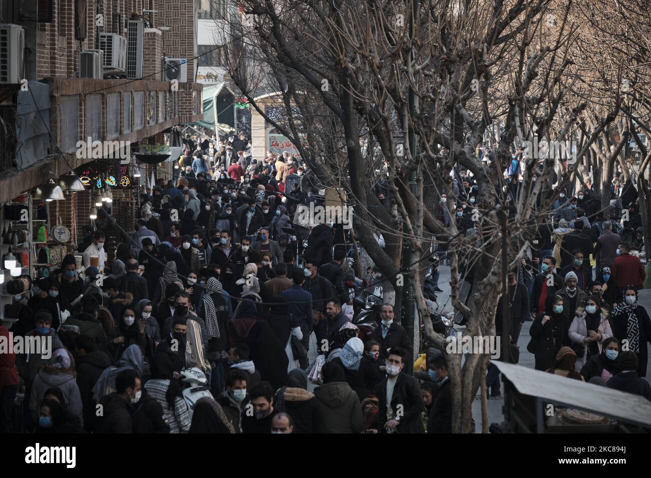 Iranian people wearing protective face masks walk along a street-side ...
