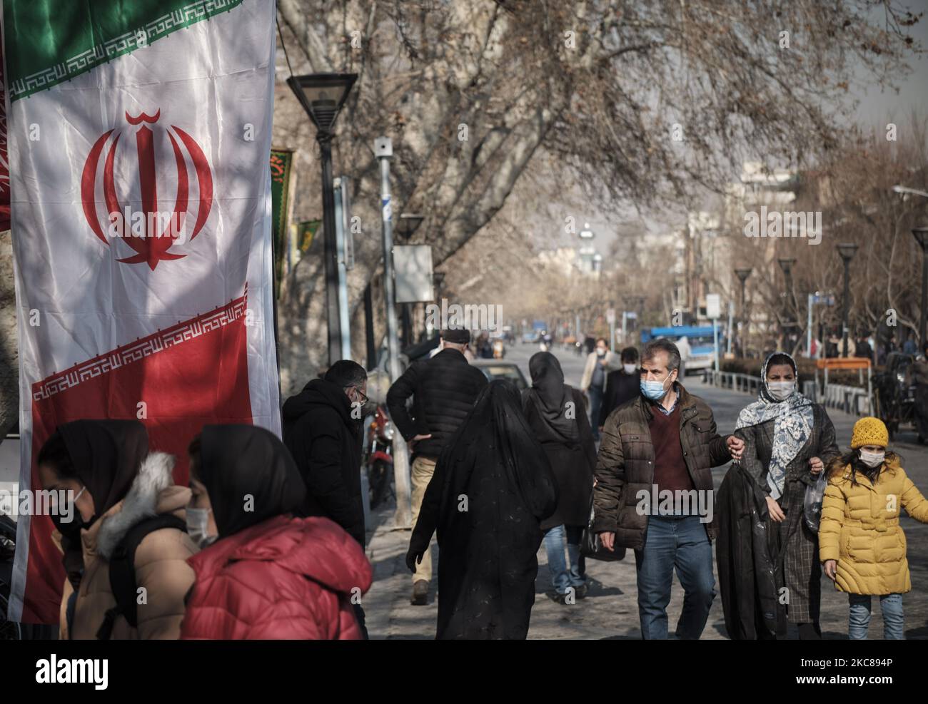 An Iranian family wearing protective face masks walk along a street ...
