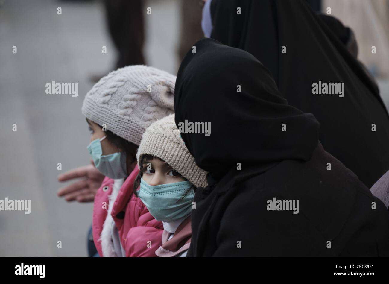An Iranian young girl wearing a protective face mask looks on as she ...