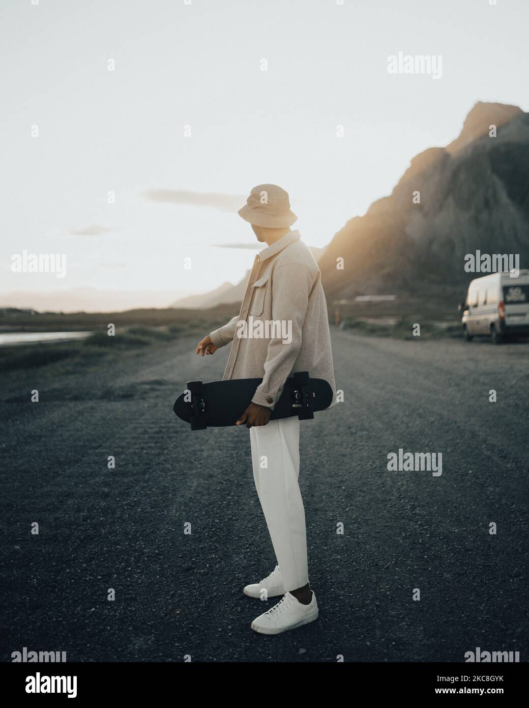 A side view of black man in fashionable outfit standing on asphalt road ...