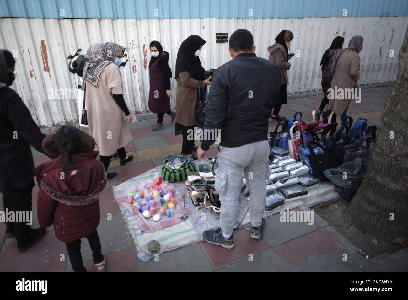 Iranian women wearing protective face masks walk past a vendor on a ...