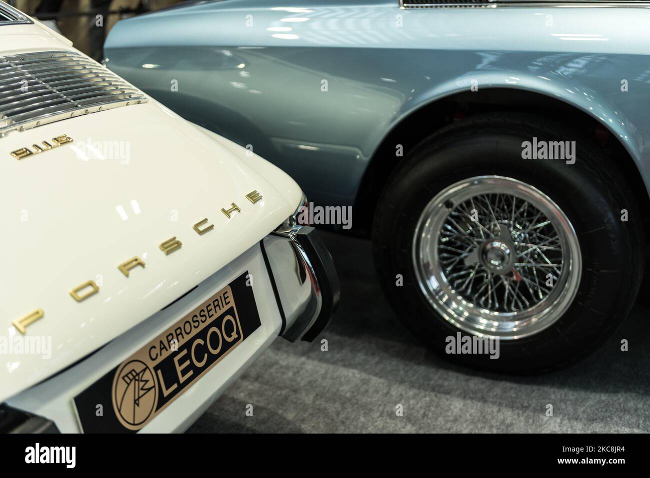 A rear view of a white vintage Porsche 911 with a light blue car in the ...