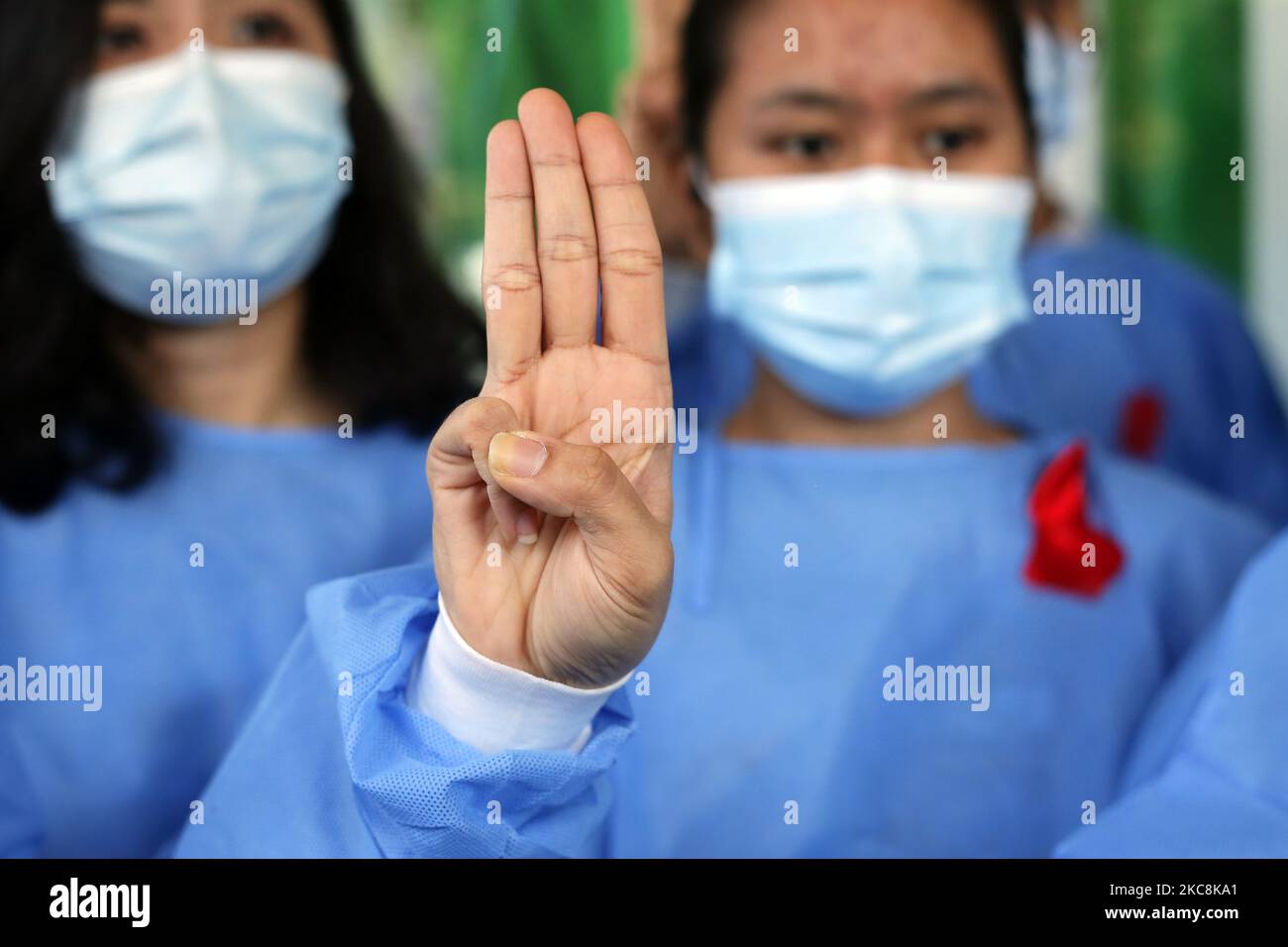A medical staff shows the three finger salute with a red ribbon on her ...