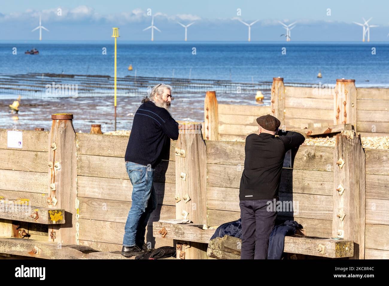 Men are seen talking on a beach in front of windmills ensuring social ...