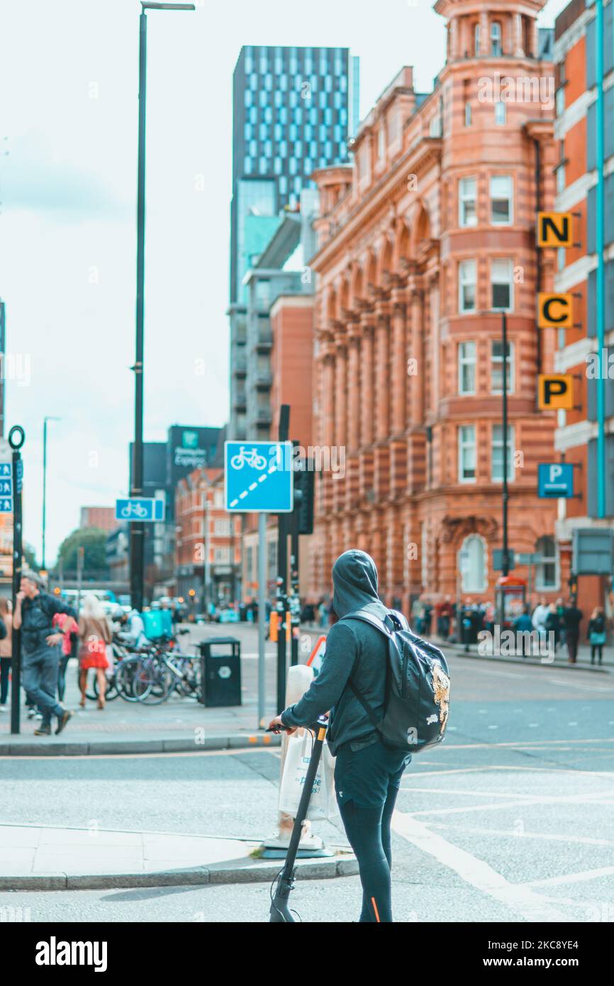 A rear view of a man riding a scooter on the street of Manchester City ...