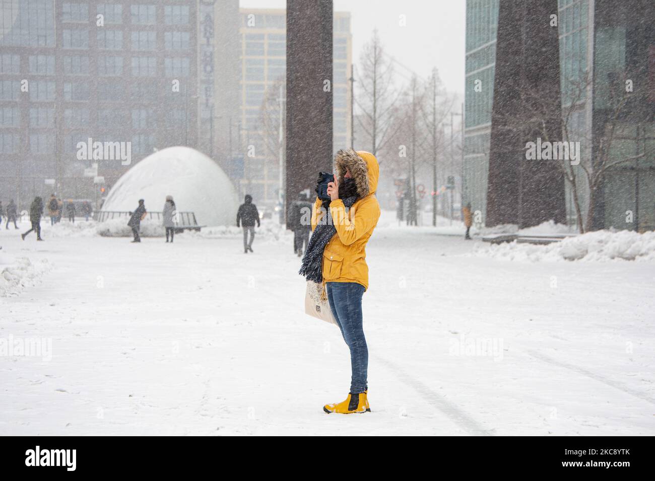 A young woman with a yellow jacket takes pictures of the snow covered ...