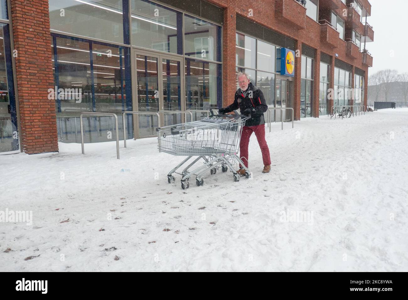 A man is carrying supermarket carriage on the snow. Blizzard from the ...