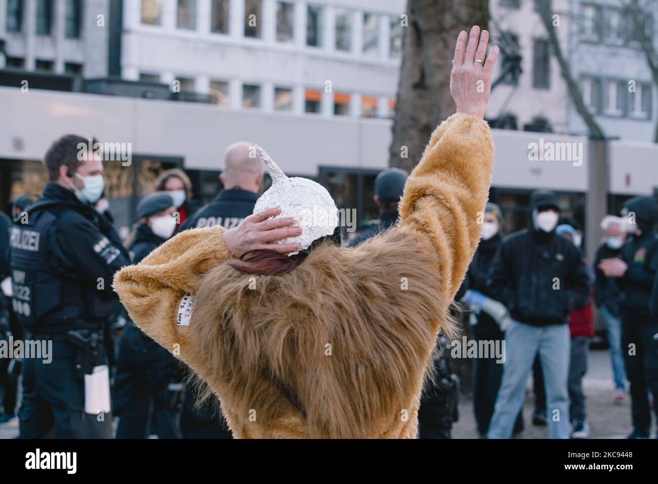 a protester from " Koeln ist Aktiv" group with tin foil hat waves and ...