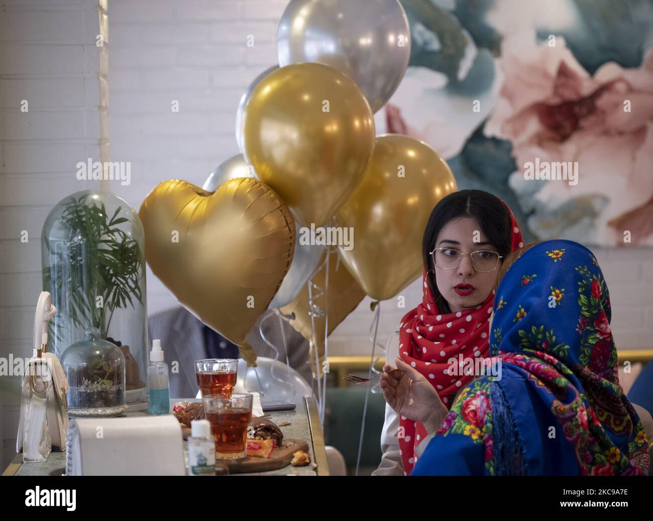 Two Iranian women talk to each other as they sit in a cafe that has decorated with balloons on ...