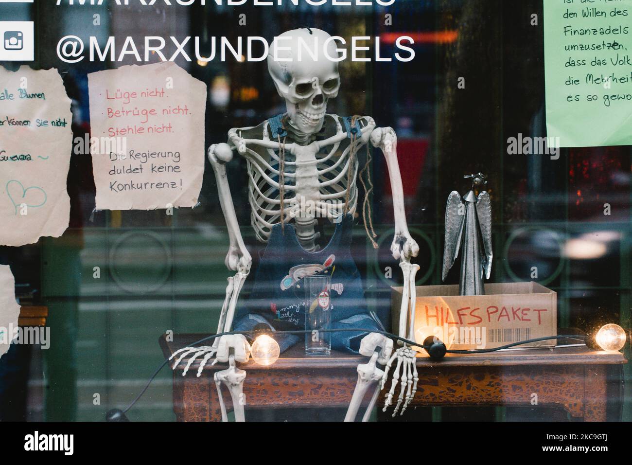a skeleton dressed as a waiter sits with a protest poster " demand help ...