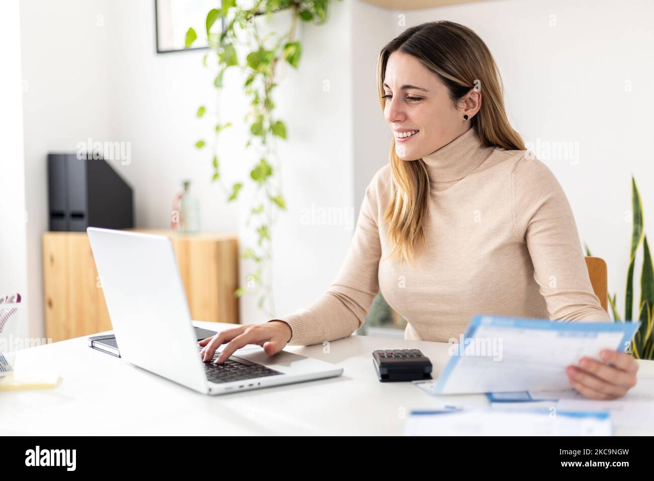 Smiling young woman consulting business invoices sitting on desk Stock ...