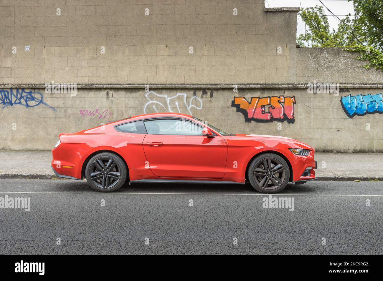 A red Ford Mustang parked in south Dublin, Ireland against a wall of ...