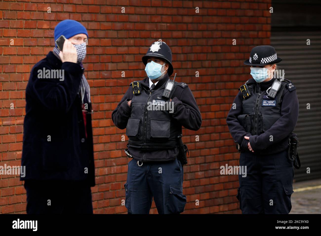A man wearing a face mask walks past police officers standing guard ...