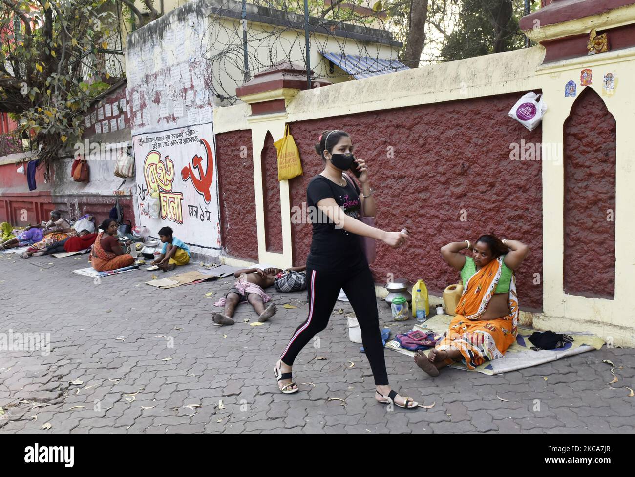 A girl talks on her phone walks past a homeless family in Kolkata ...