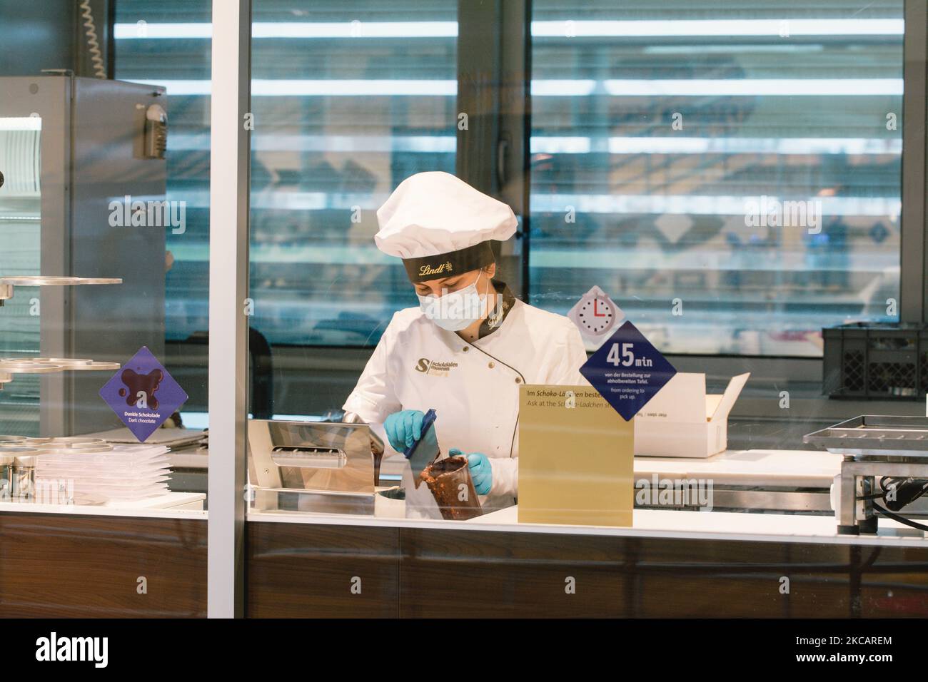 a staff with face mask makes chocolate inside the plexiglass room ...