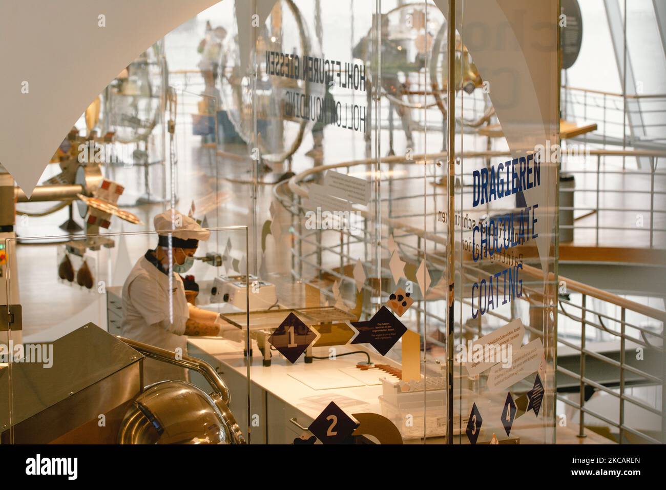 a staff with face mask makes chocolate inside the plexiglass room ...