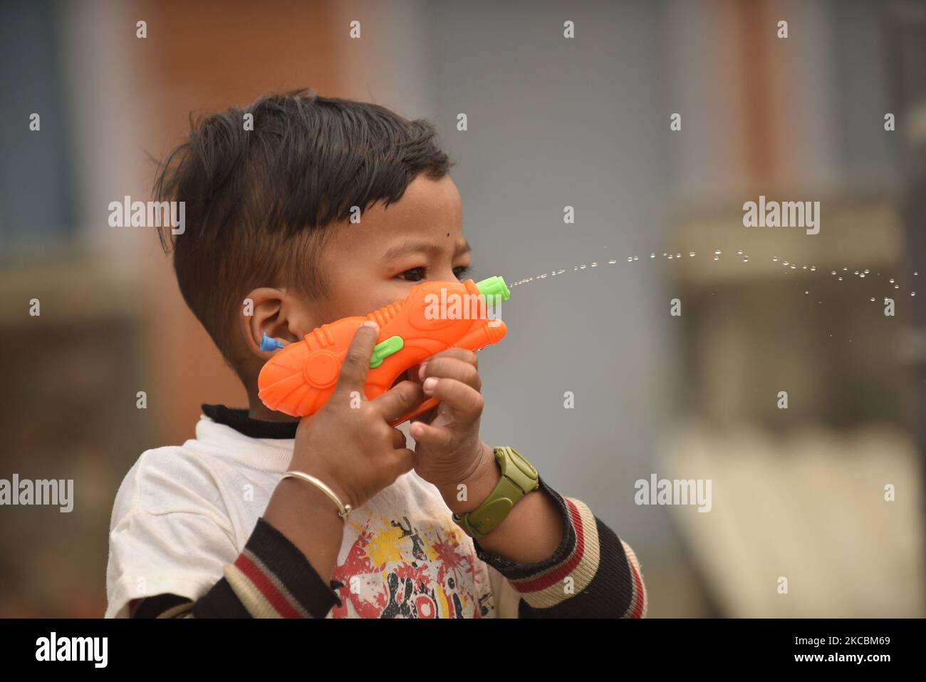 A little kid using water gun to spray water during Holi or Fagu Purnima ...