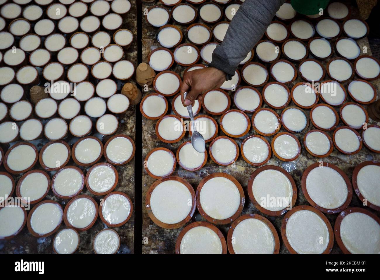 A hand of a man is seen as he pours milk into the earthen containers to ...