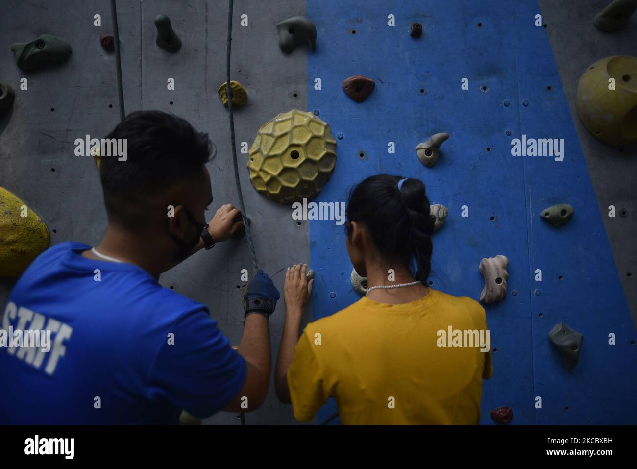 A staff helps by giving directions and guiding him to holds on the ...