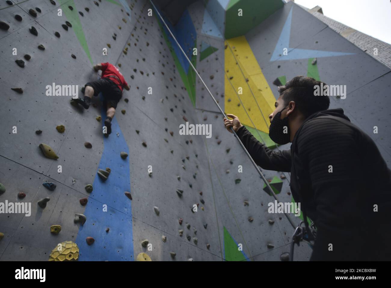 A staff helps by giving directions and guiding him to holds on the ...