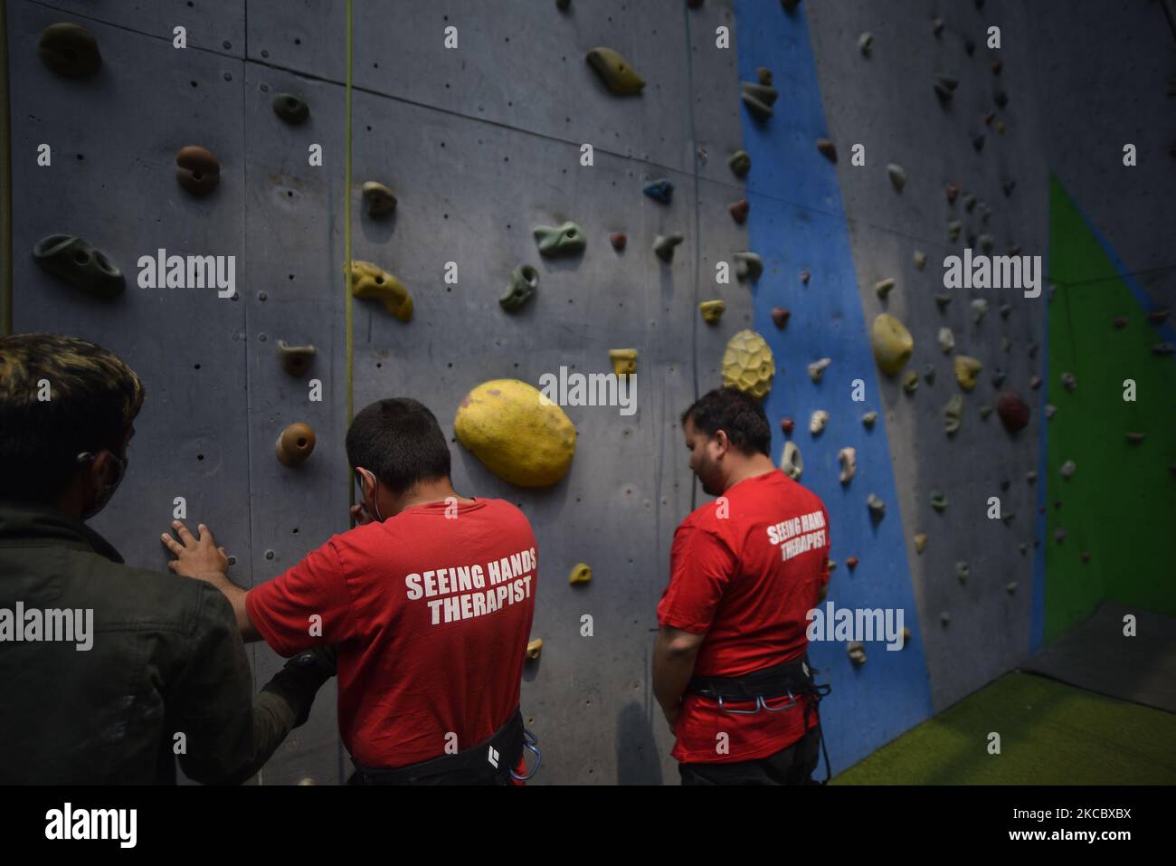 A staff helps by giving directions and guiding him to holds on the ...