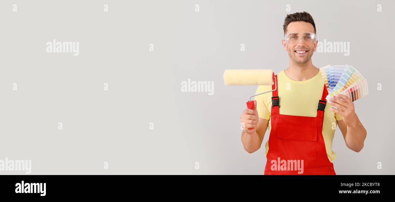 Male painter with roller and color samples on light background with ...