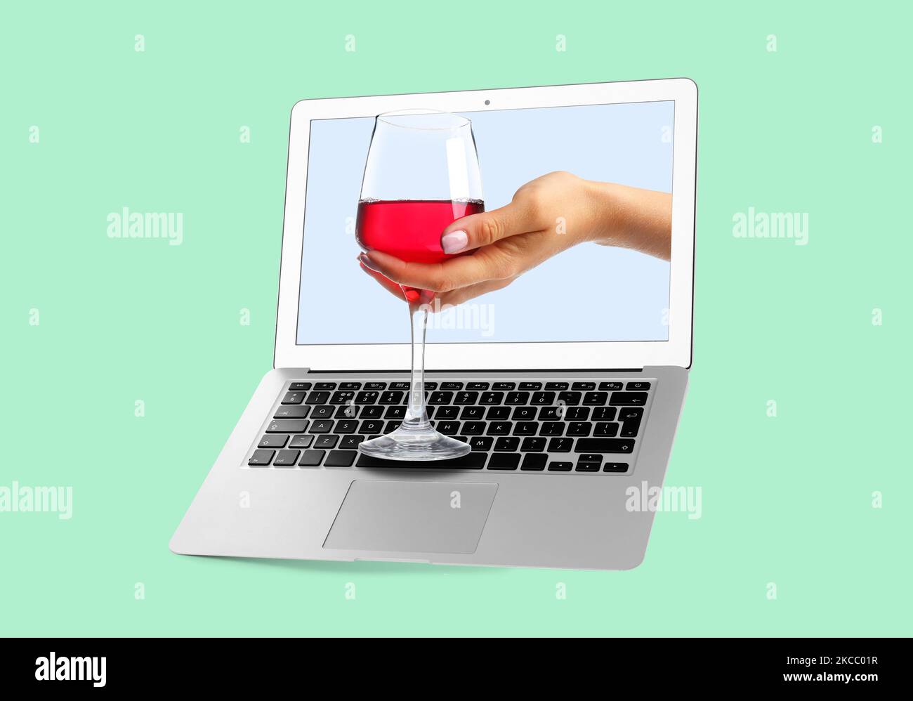 Female hand holding glass of red wine through screen of laptop on green ...