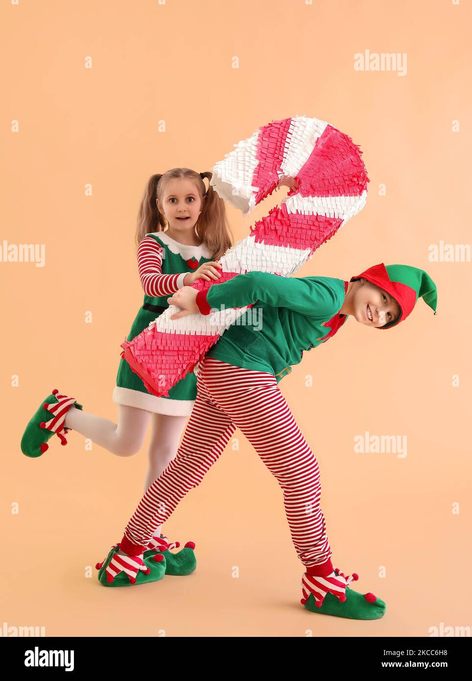 Little children dressed as elves with candy cane pinata on beige ...
