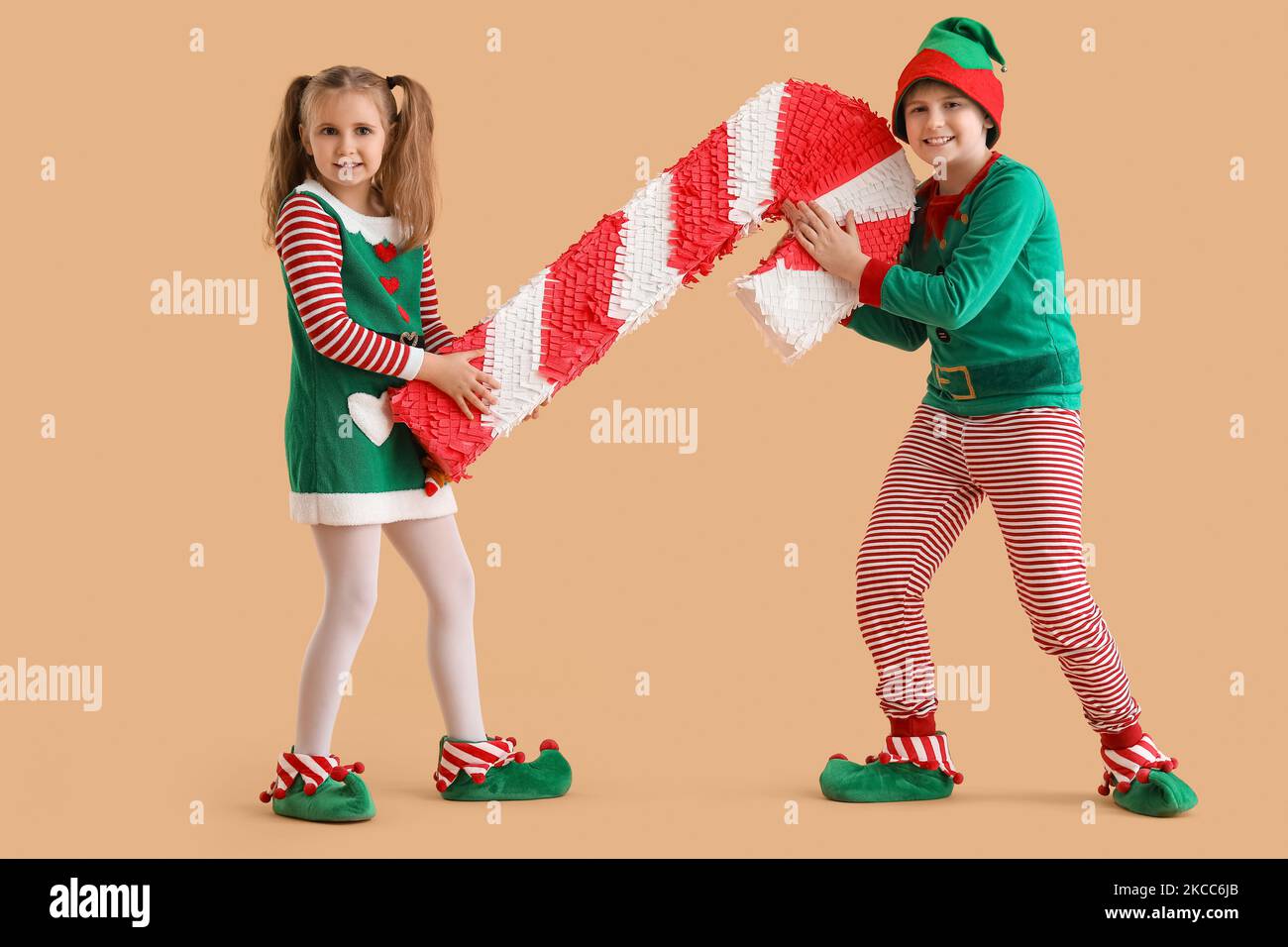 Little children dressed as elves with candy cane pinata on beige ...