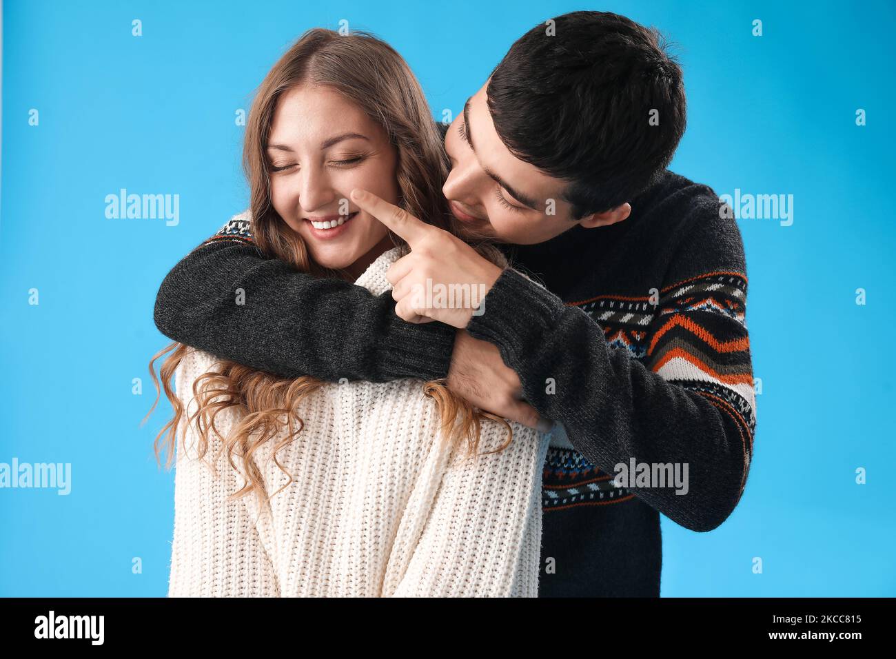 Loving couple in warm sweaters hugging on blue background Stock Photo ...