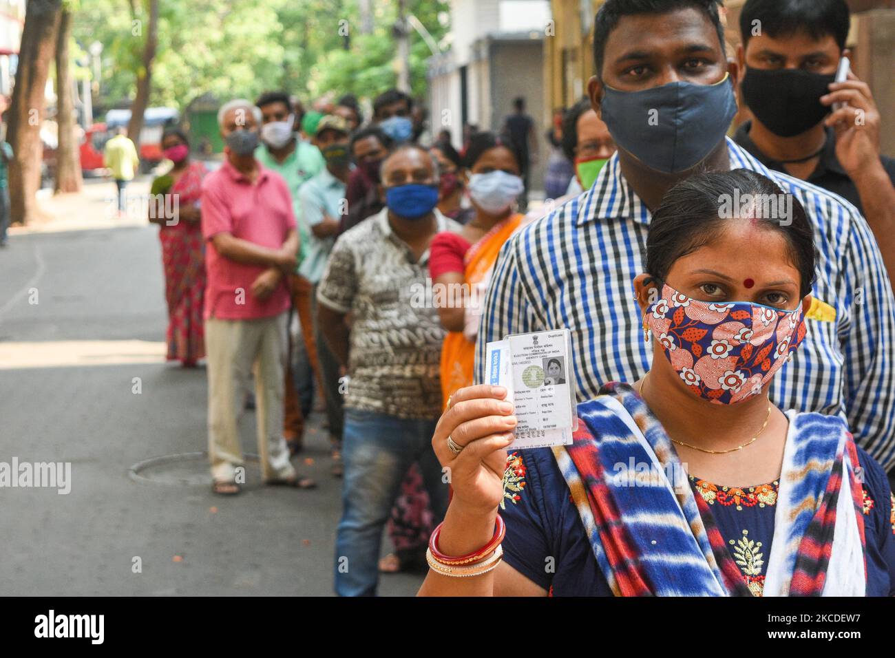 A lady wearing mask shows her voter id card as she queued in front of a ...