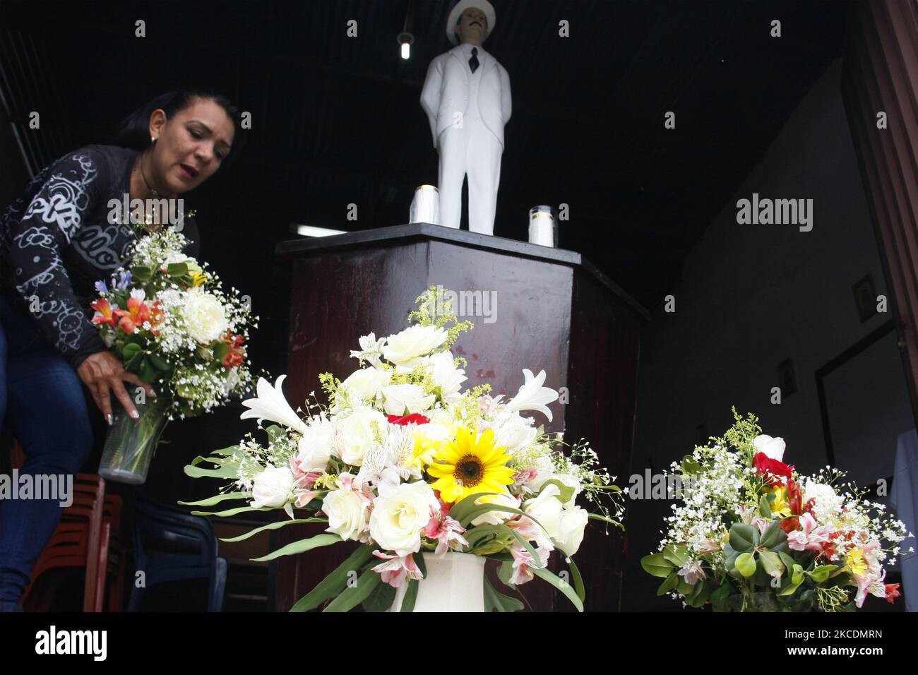 A woman places flowers on an altar raised at the entrance of a home in ...