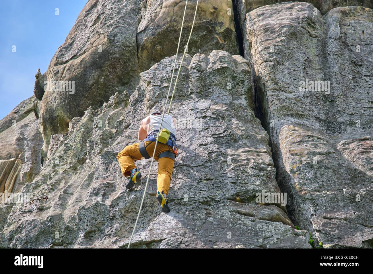 Determined climber clambering up steep wall of rocky mountain ...