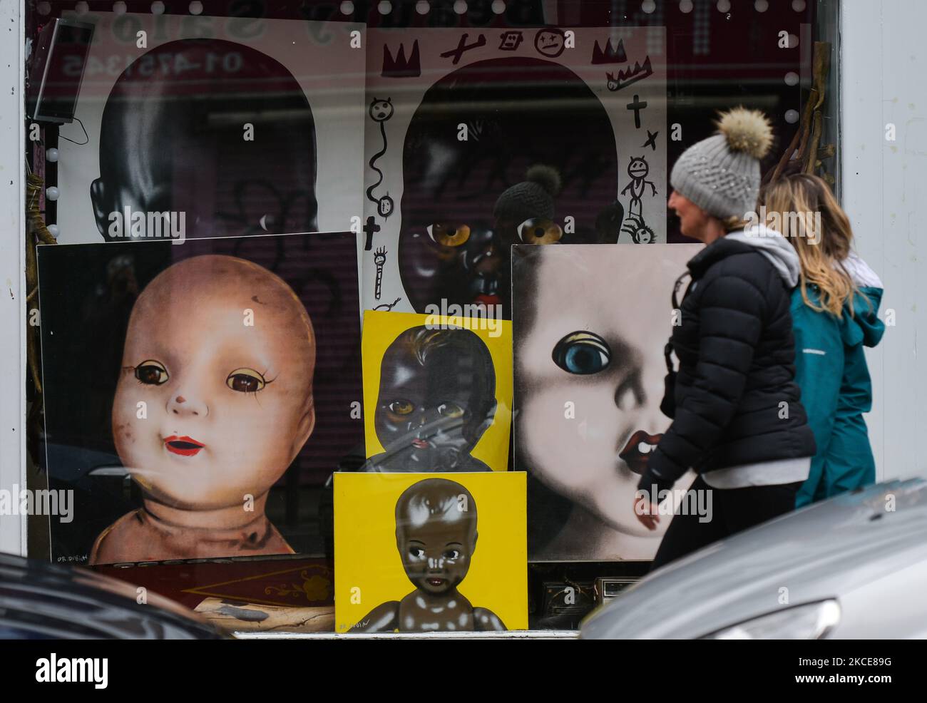 Two women walk by images of children seen in the window of a closed Art ...