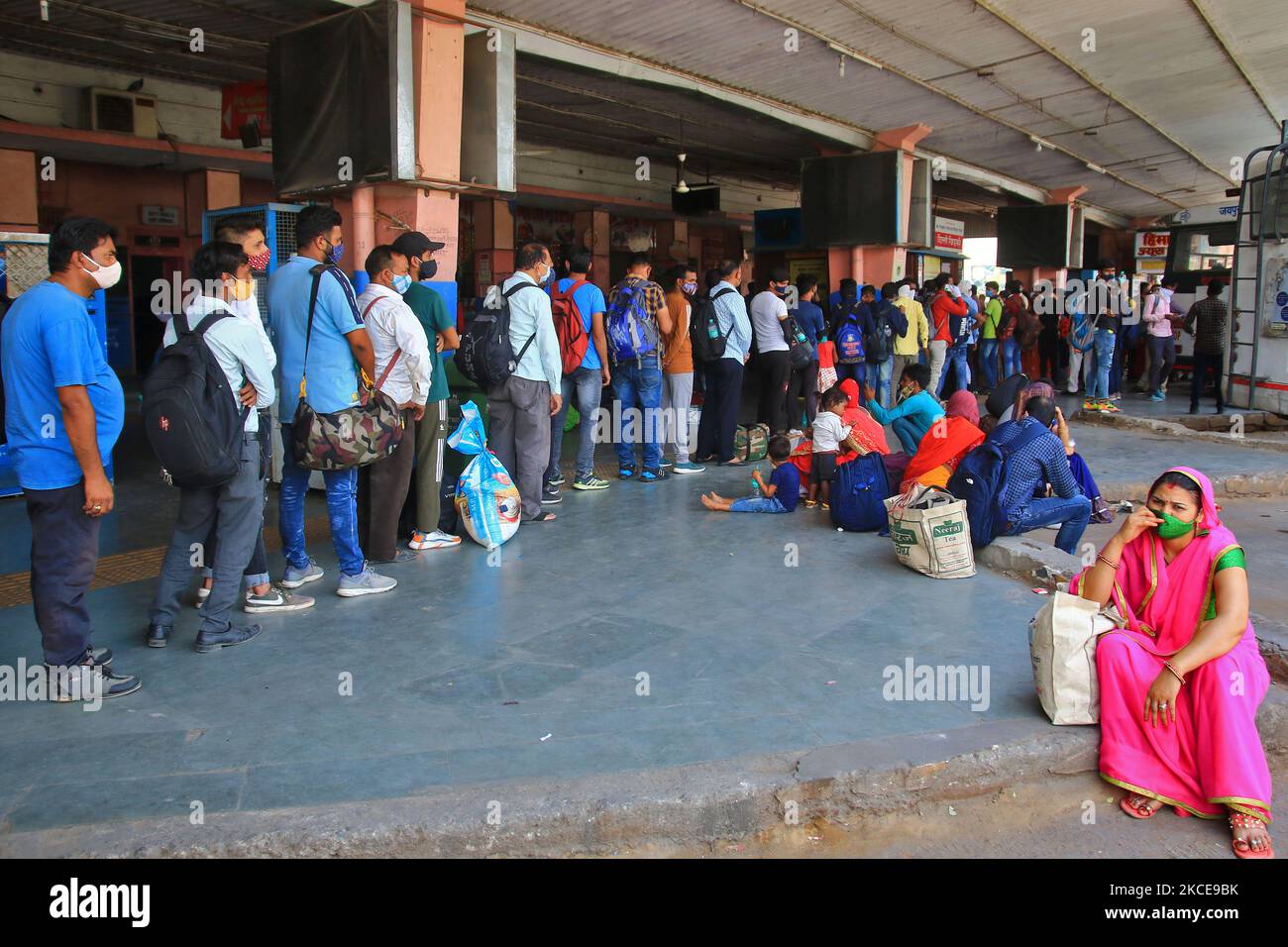 Passengers stand in a queue at a ticket counter to board buses for ...