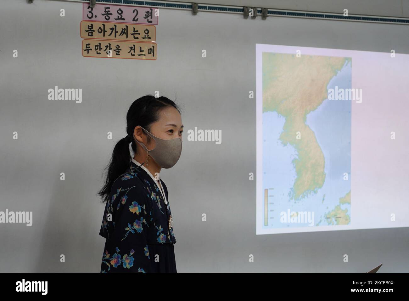 A teacher wearing a face mask and a Korean traditional dress conducts a ...