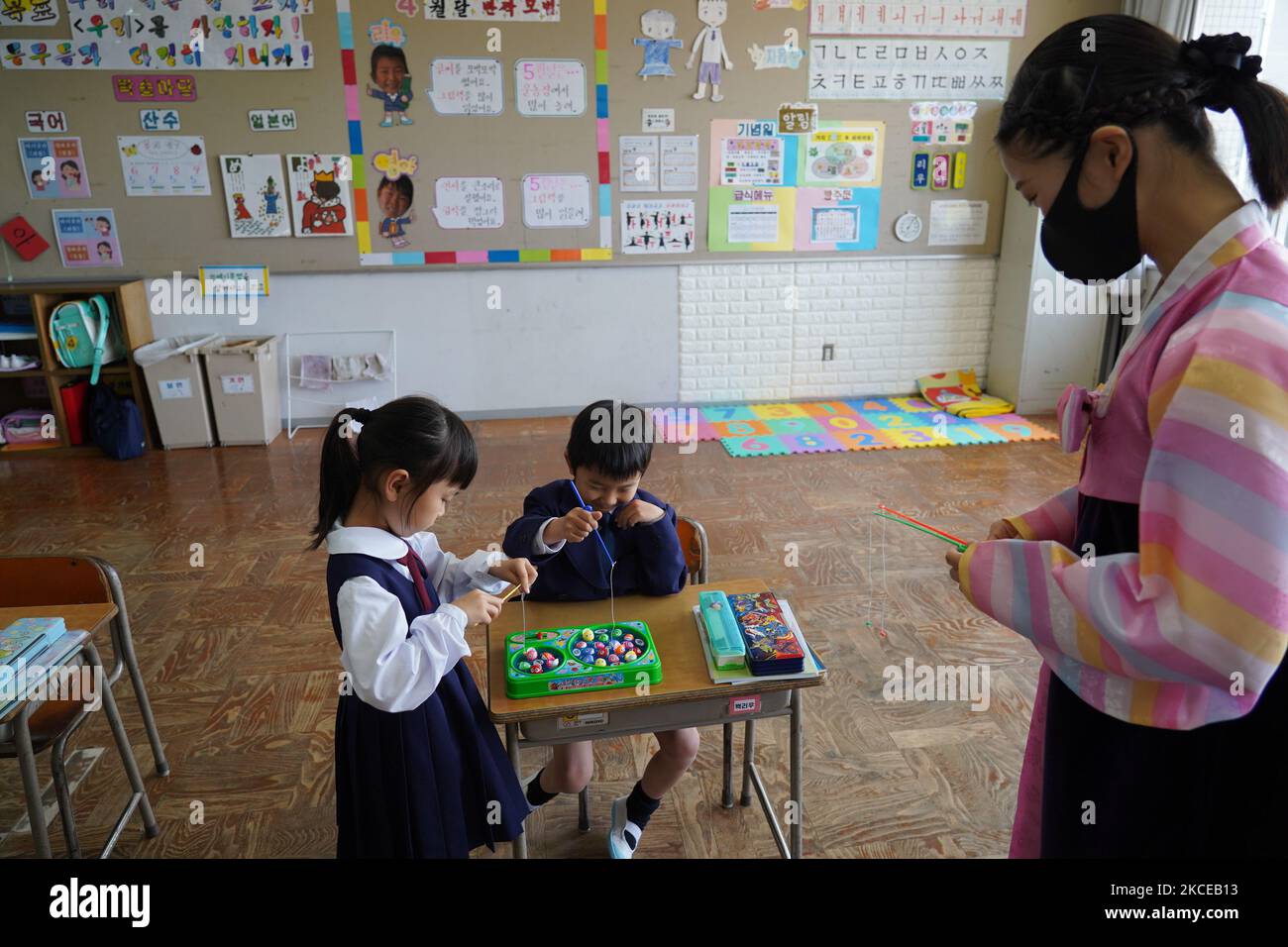 Elementary students play fishing game as a teacher wearing a Korean ...
