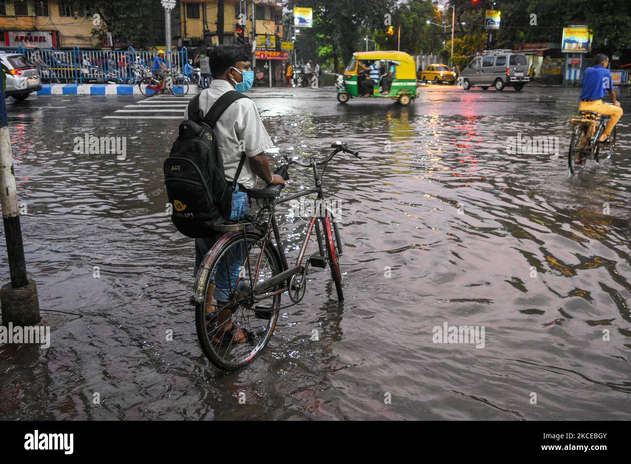 A gentleman wearing mask waits to cross a flooded road after heavy ...
