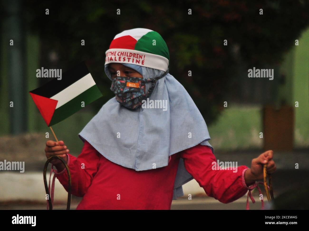 A child wearing a mask, holds a small Palestine flag during a ...