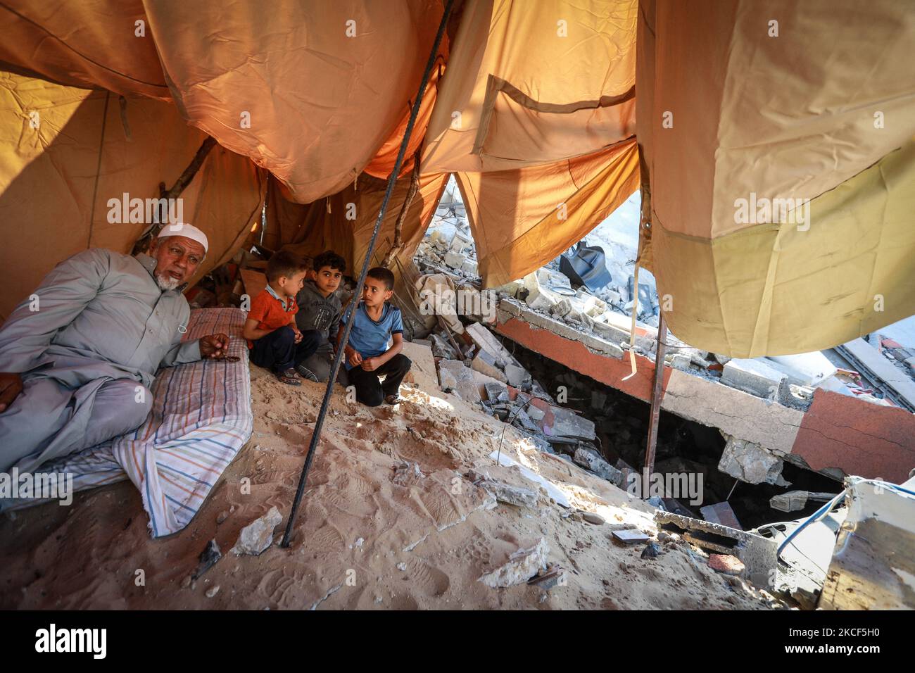 Palestinians sit in a makeshift tent amid the rubble of their houses ...